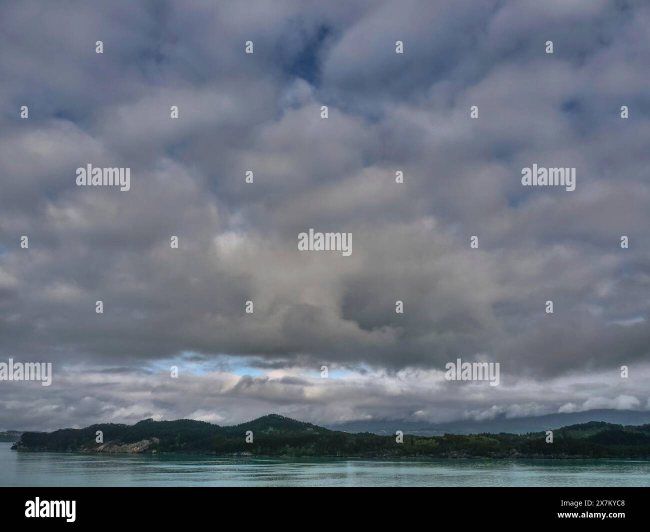 Wide cloud cover over a calm body of water, with gentle mountains on the horizon, greenish ...