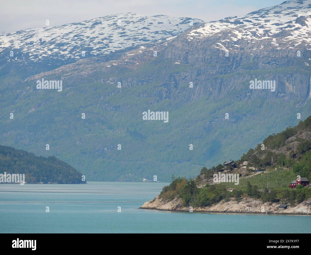 A calm lakeshore with mountains and wooded hills, under a clear blue ...