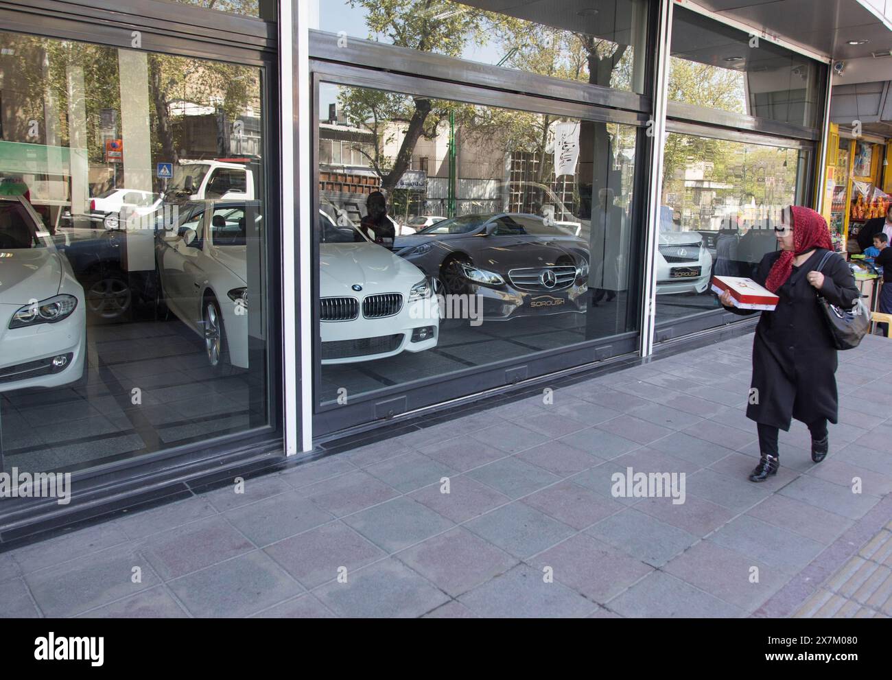 A woman walks past a car dealership with BMW and Mercedes cars in ...