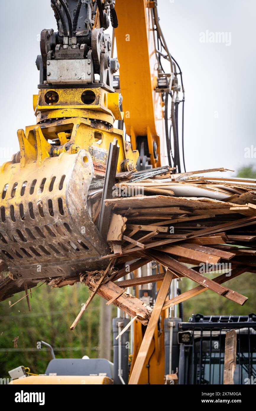 Excavator with large metal grapple crushing a pile of wood and moving ...