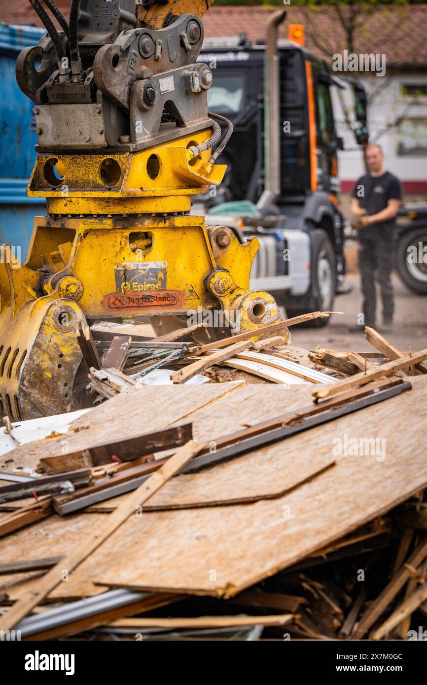 An excavator piles wood debris next to a lorry while a worker stands ...