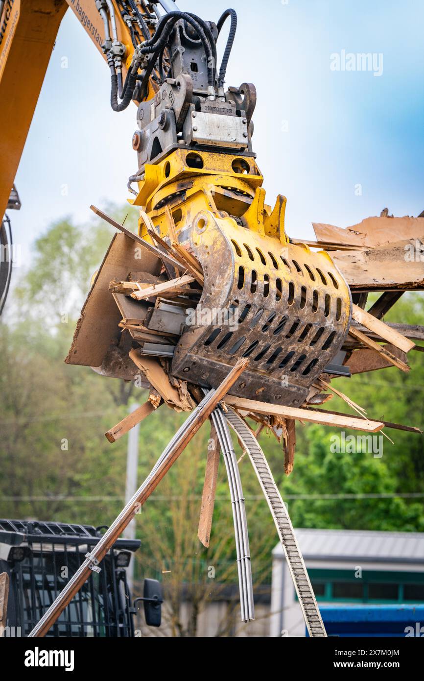 Hydraulic grab on an excavator lifts piles of wood against a green ...
