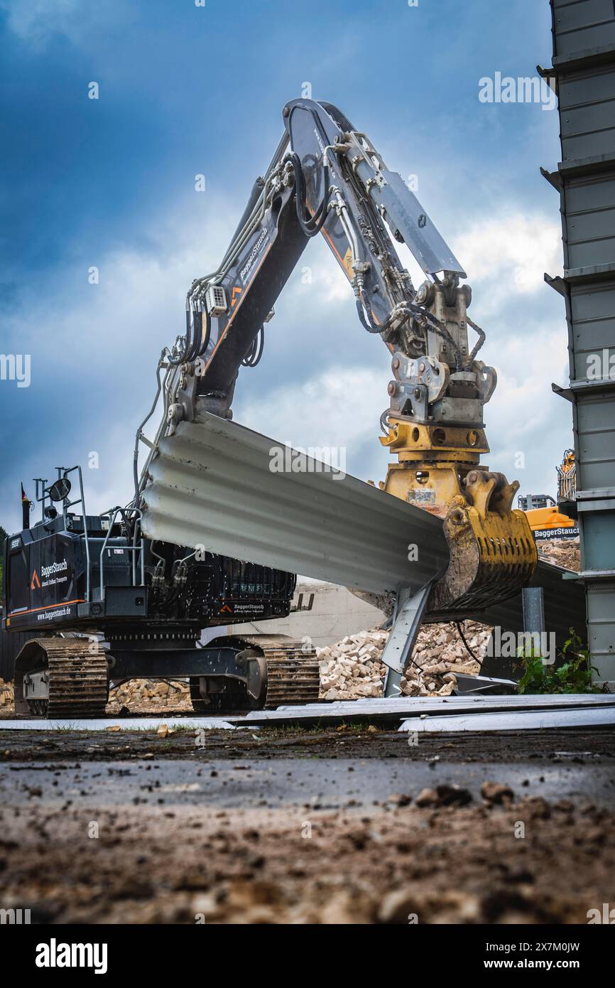 A large excavator lifts building materials on a construction site, the ...