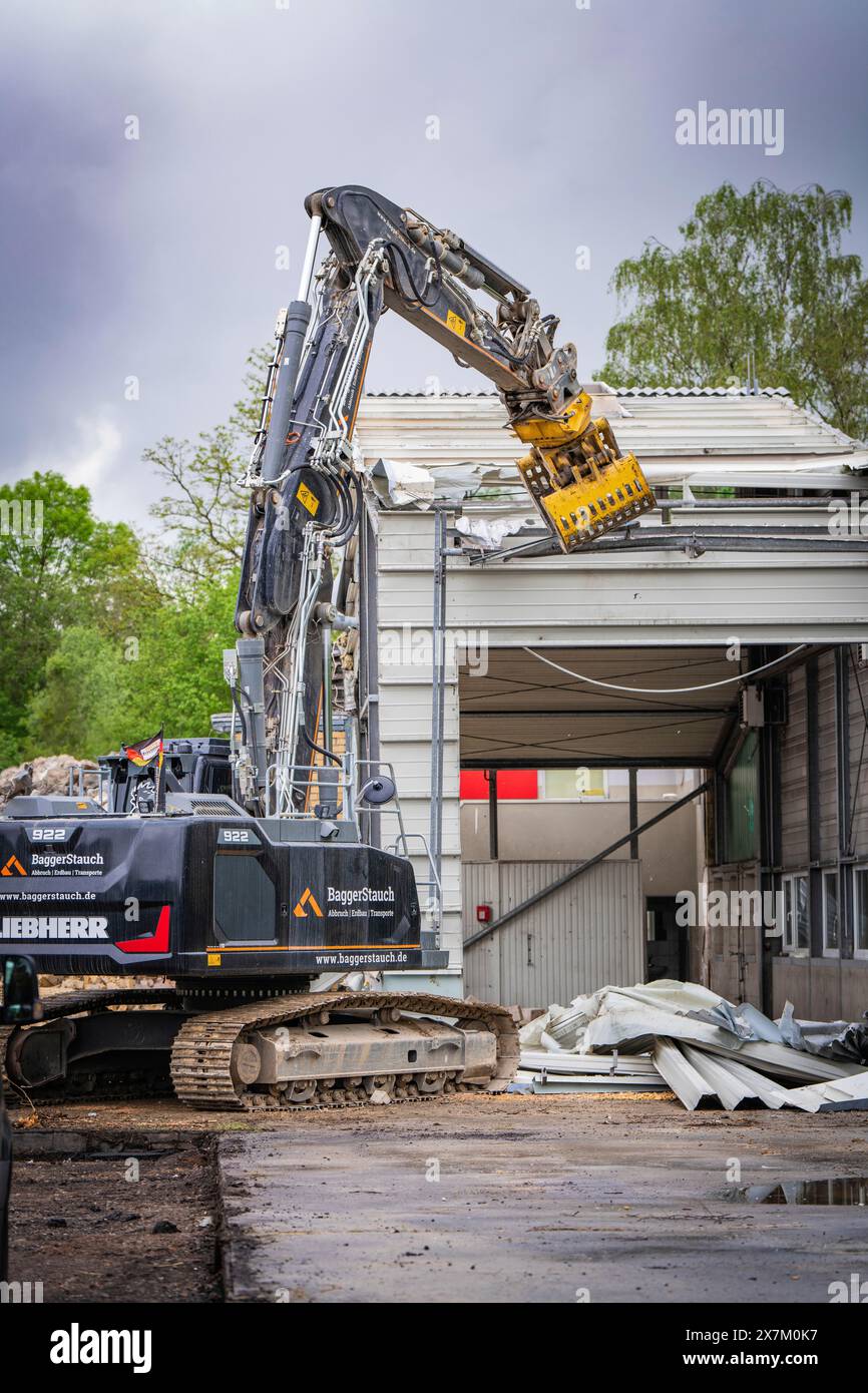 An excavator demolishes a building outside under a cloudy sky ...