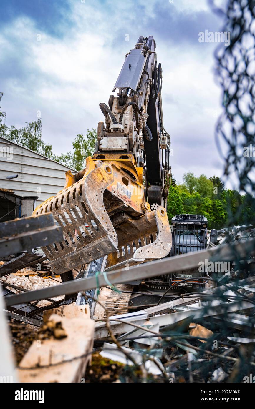 An excavator's metal tongs move rubble and debris in a construction site with green background ...