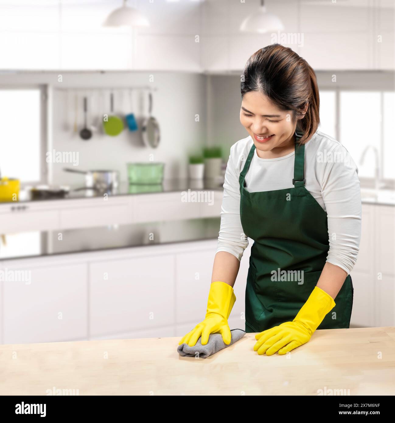 Asian housekeeper wear yellow rubber gloves and green apron wipe table ...