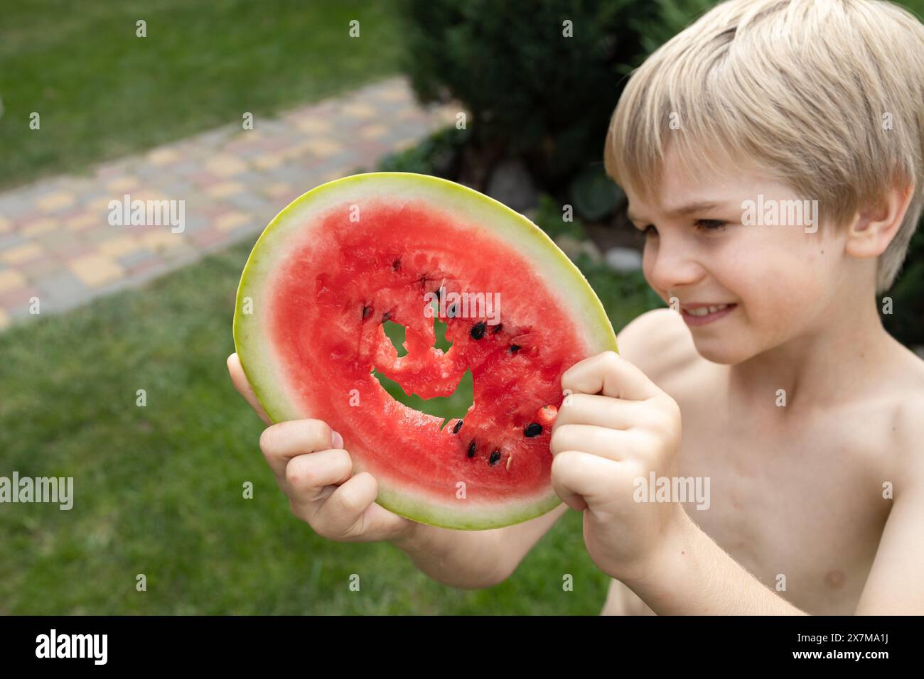 boy happily eats a watermelon, carving a smile in a round piece of ...