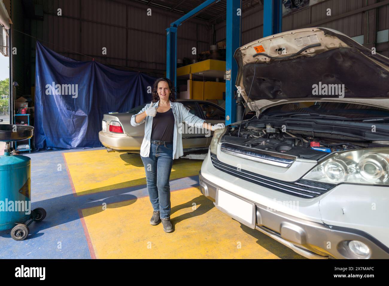 Auto repair shop owner stands in a garage with an open car hood and ...