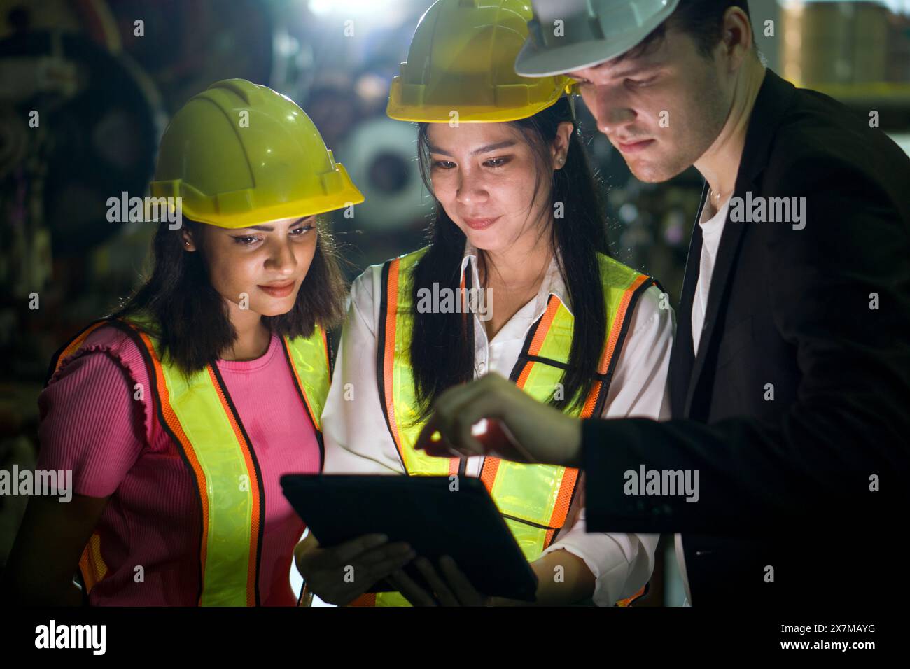 Three worker wearing safety vest and helmet are looking at a tablet ...