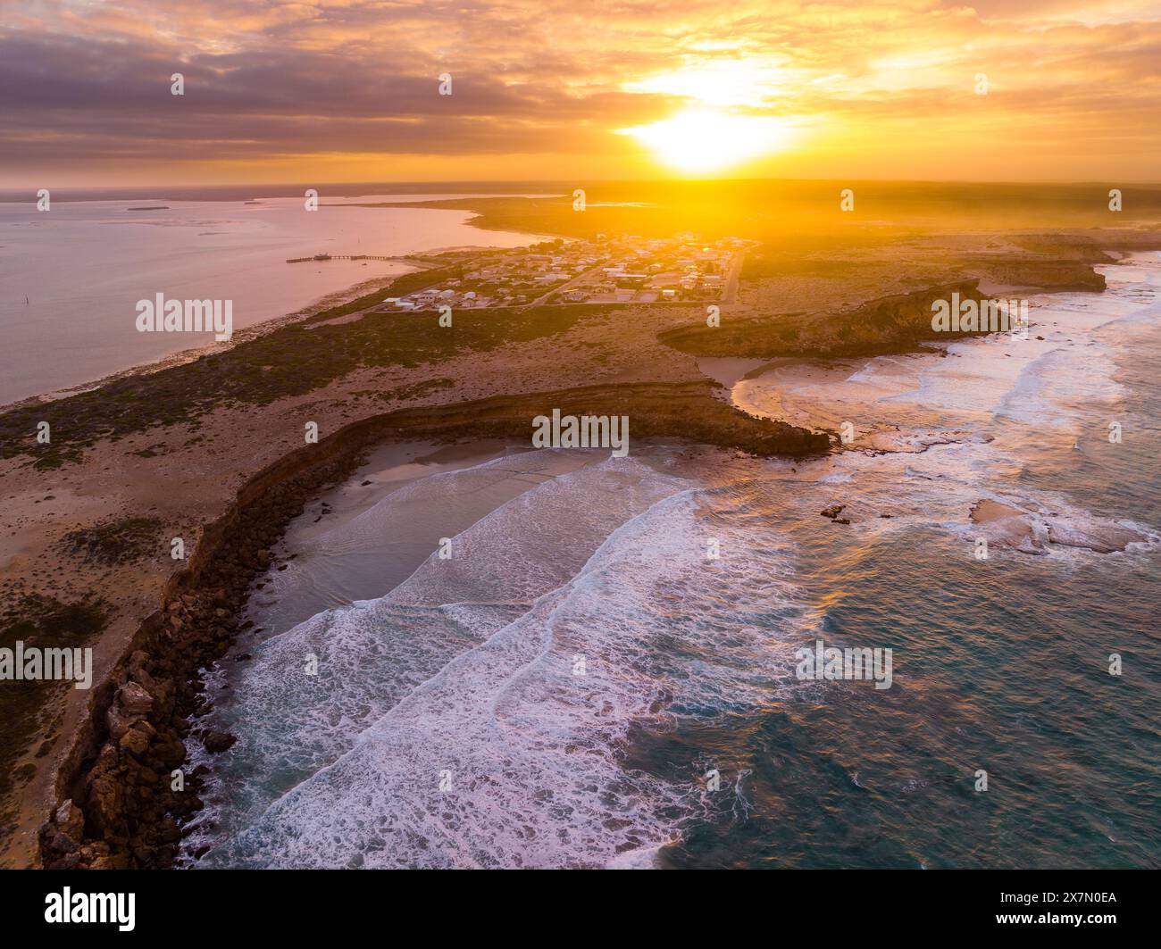 Aerial view of a hazy sunrise over a small township on a rugged coastal ...