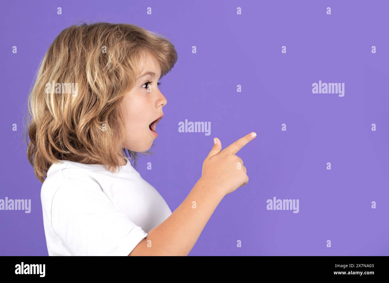 Surprised kid looking away, pointing finger on isolated studio ...