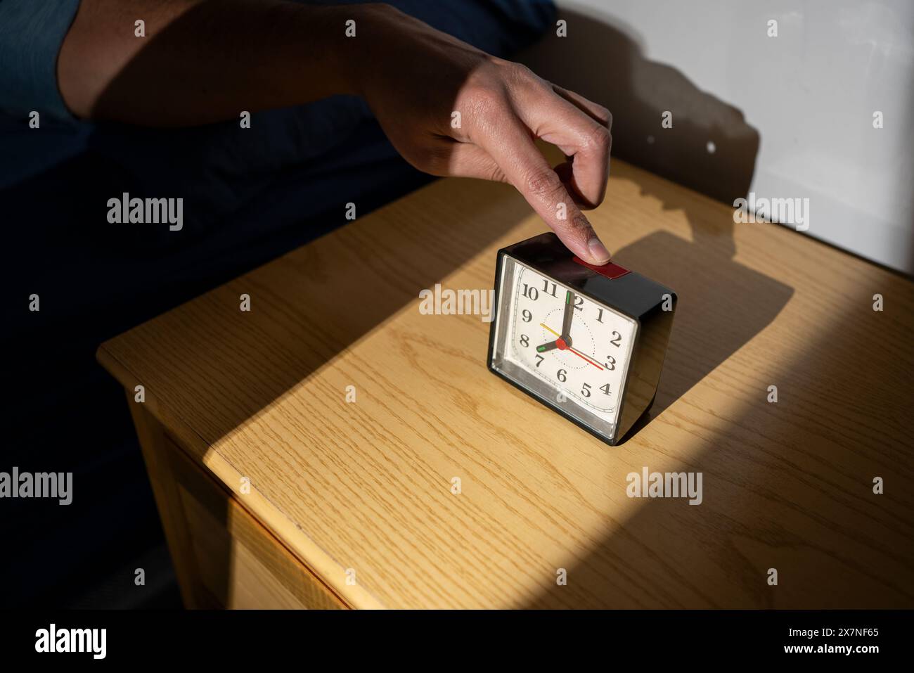 Young man reaching for his alarm clock after waking up in bed at home ...