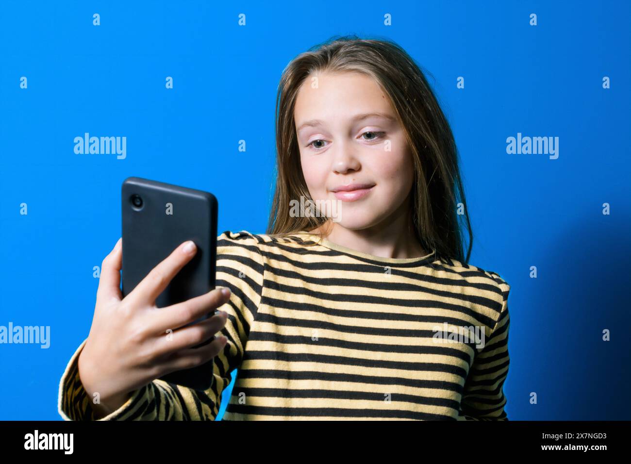 A teenage girl takes a selfie on her phone. Close-up portrait. Blue ...