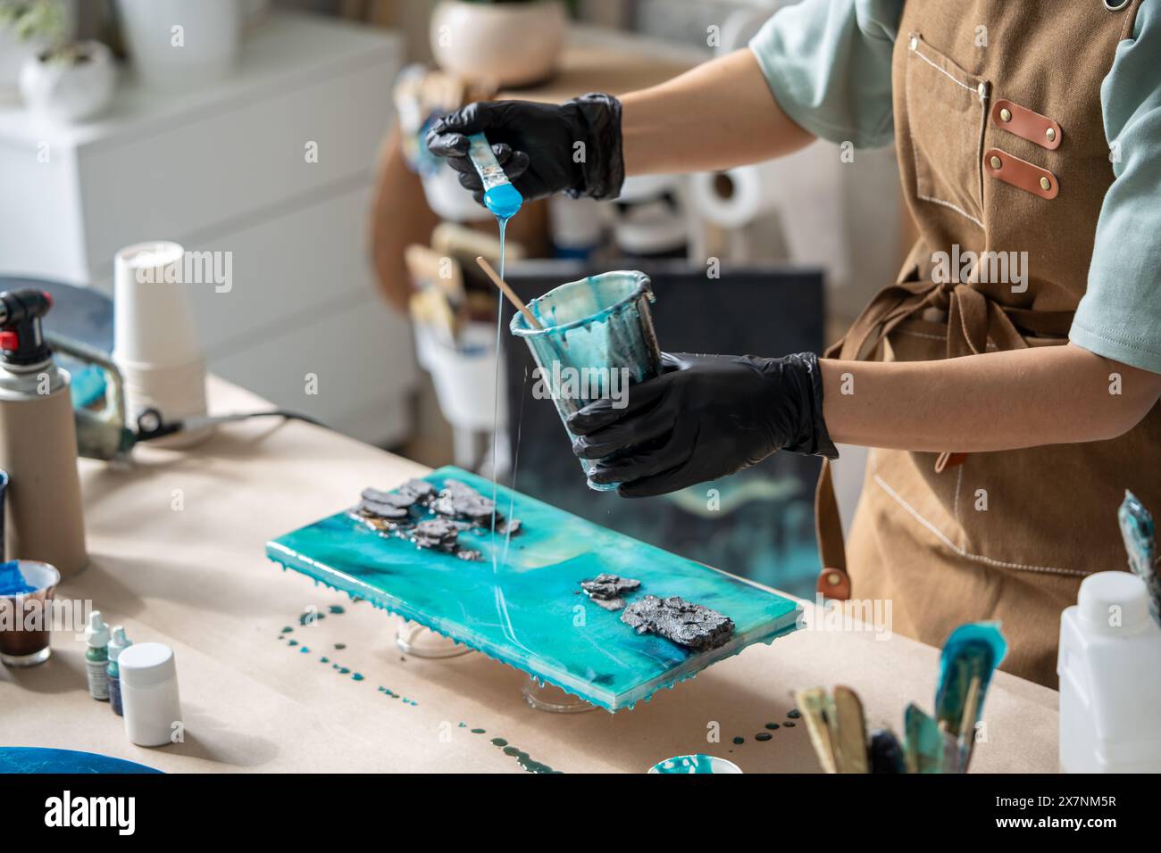 Woman artist pours epoxy resin and smears it with stick on wooden board ...