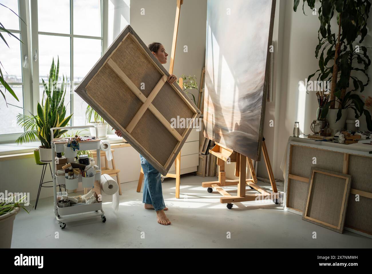 Creative female artist stands in art studio, holding large canvas looks ...