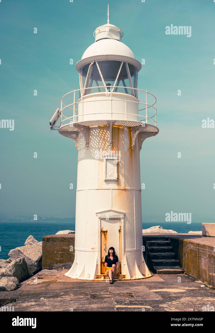 Woman in black and yellow sitting at the foot of a white lighthouse ...