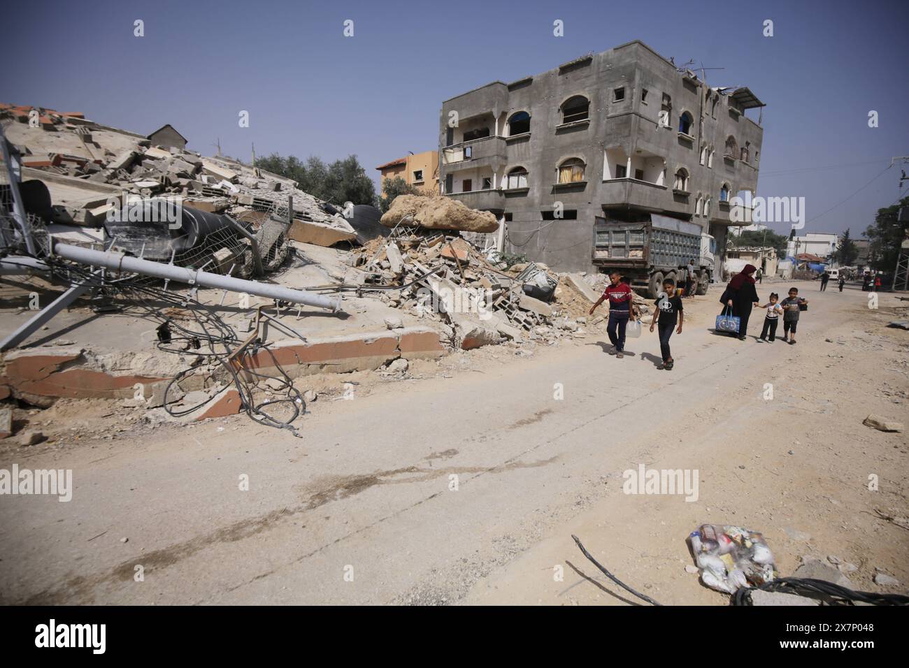 Displaced Palestinians walk between buildings destroyed in Israeli ...