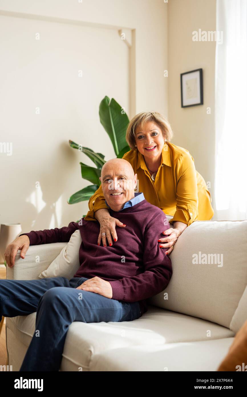 An elderly smiling couple together in a cozy, sunlit living room. The ...