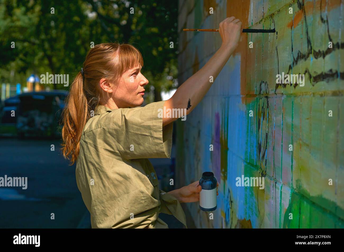 Pretty graffiti artist painter with a brush on a stepladder paints a wall Stock Photo - Alamy