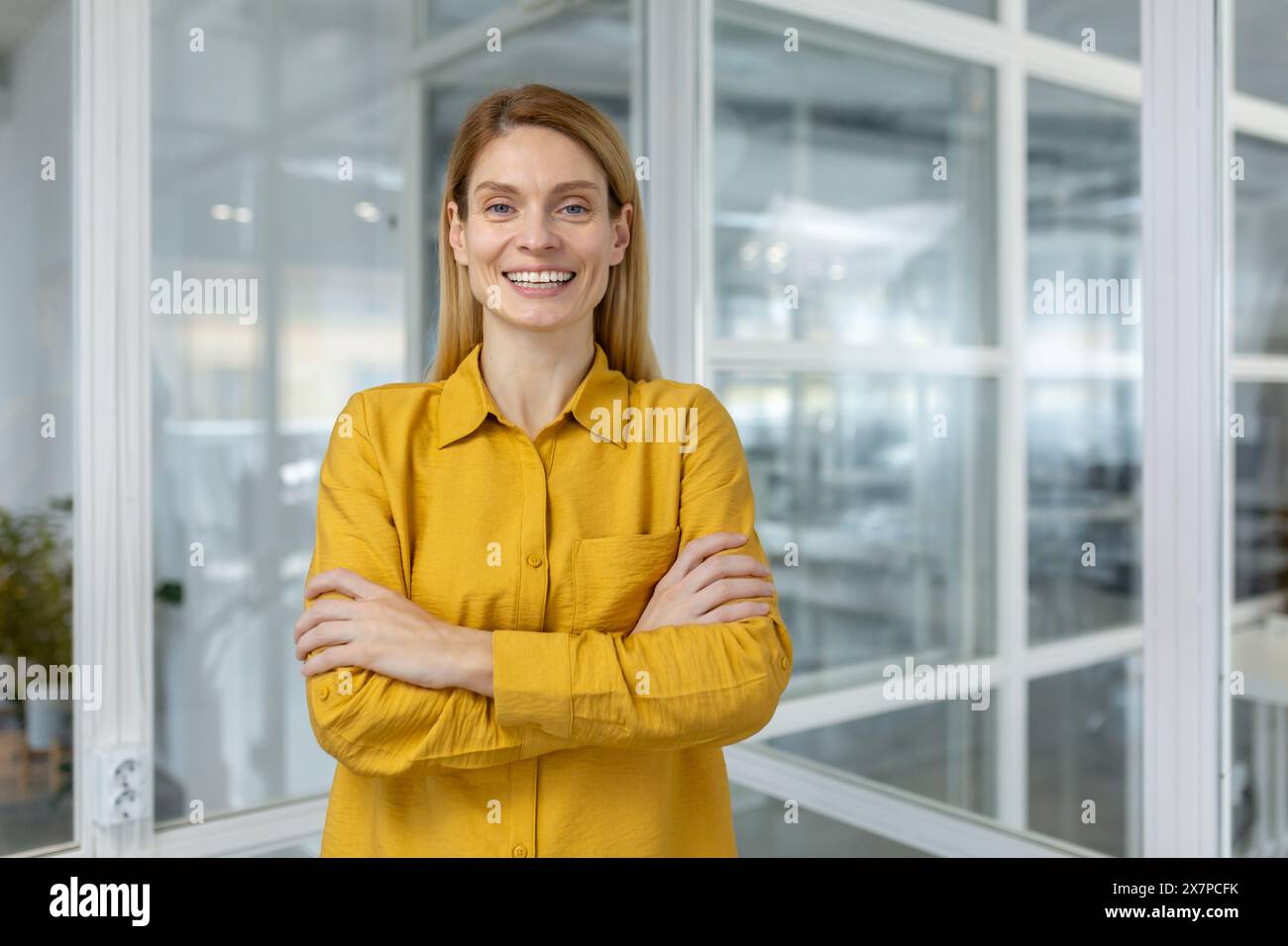 Smiling businesswoman standing with arms crossed in a modern office ...