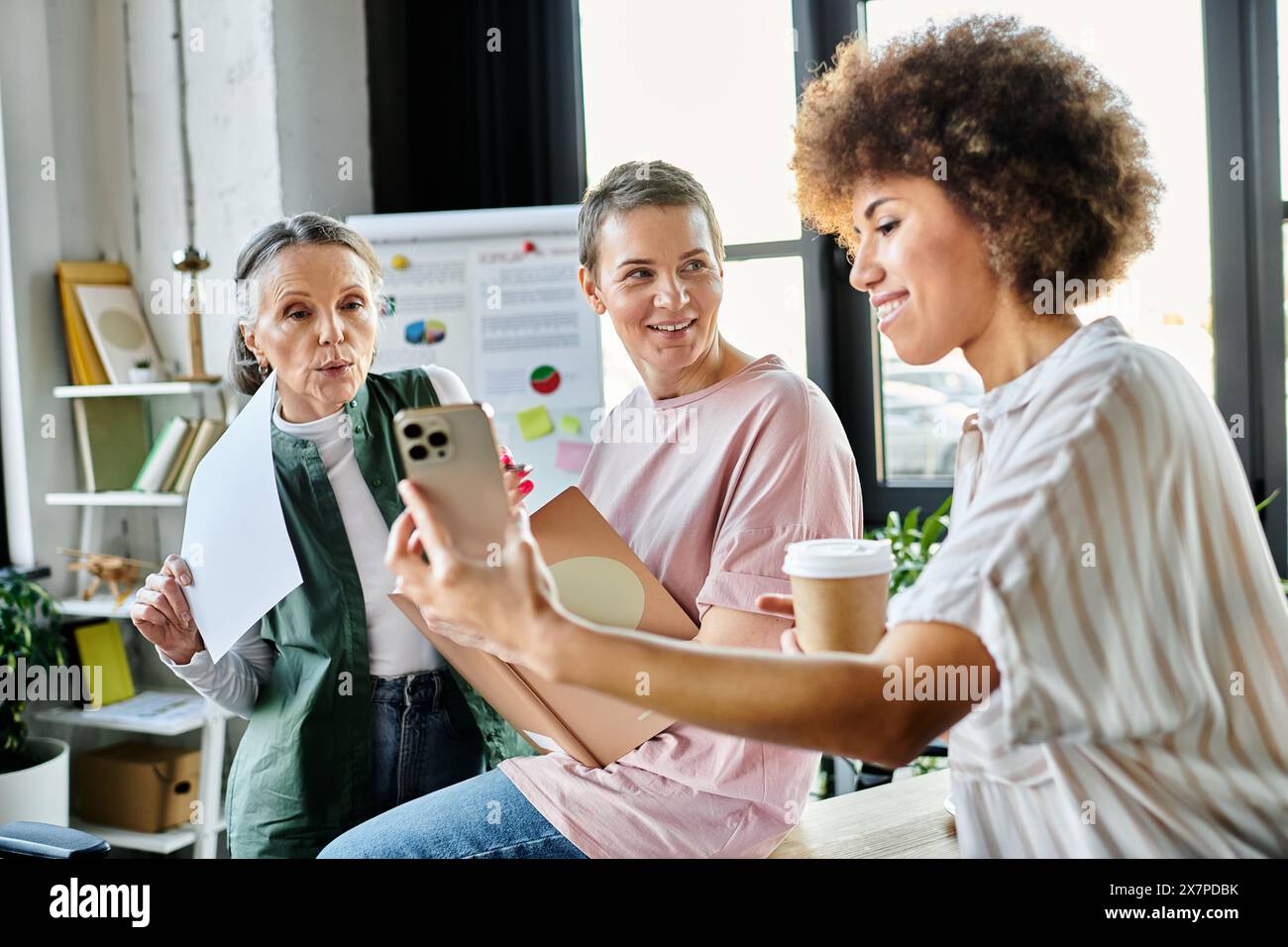 Diverse businesswomen engaged around table with cell phone Stock Photo ... Diverse businesswomen engaged around table with cell phone Stock Photo ...