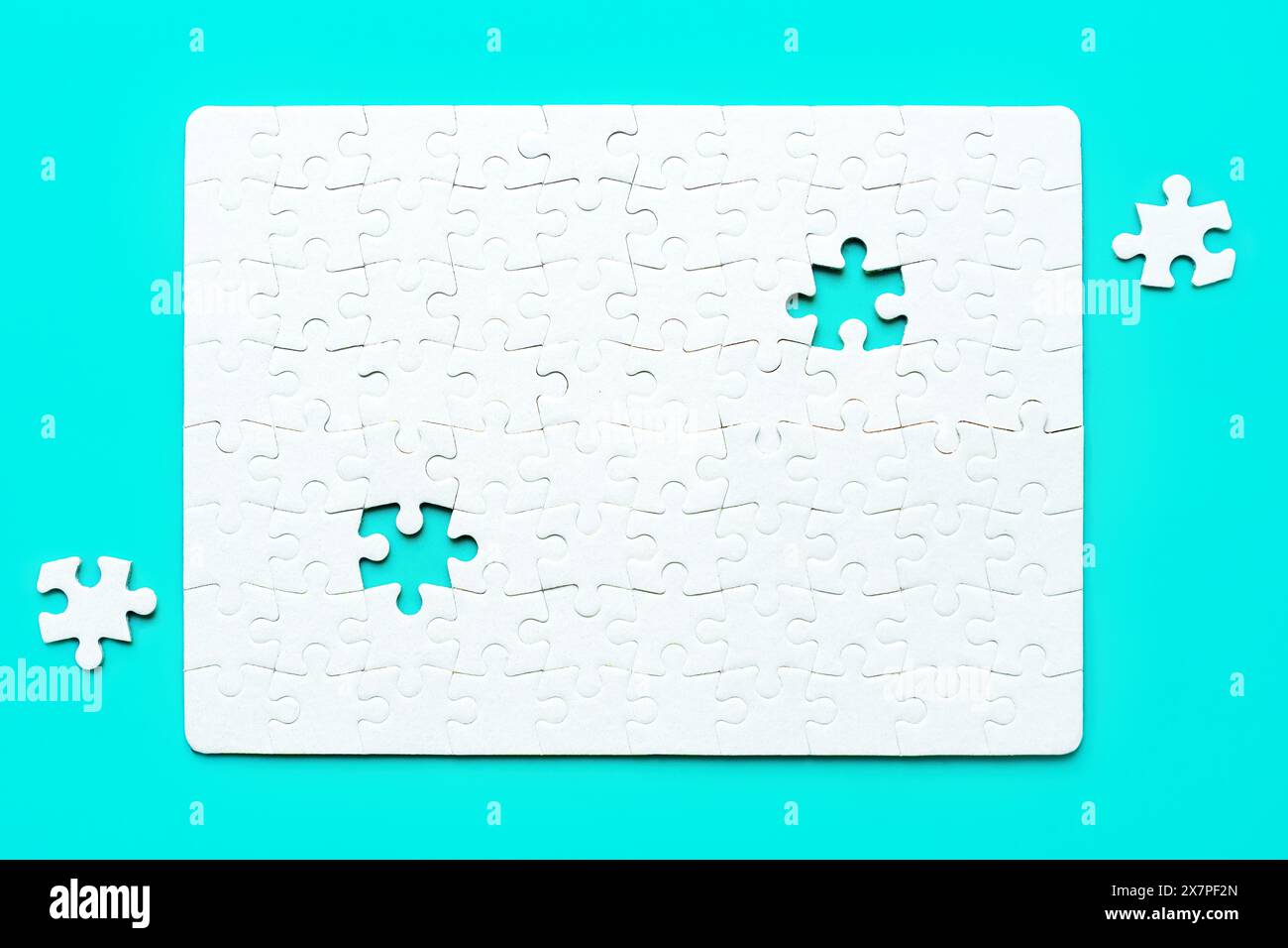 Blank white rectangular puzzle with two final pieces set aside on a ...