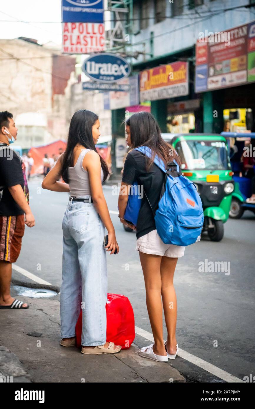 Two young filipino girlfriends wait for a bus or jeepney in the Tondo ...