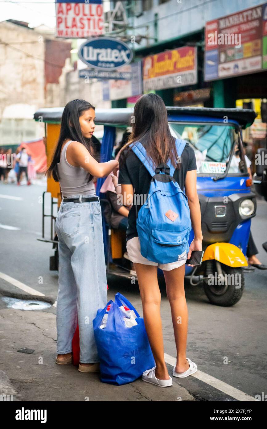 Two young filipino girlfriends wait for a bus or jeepney in the Tondo District Manila, The ...