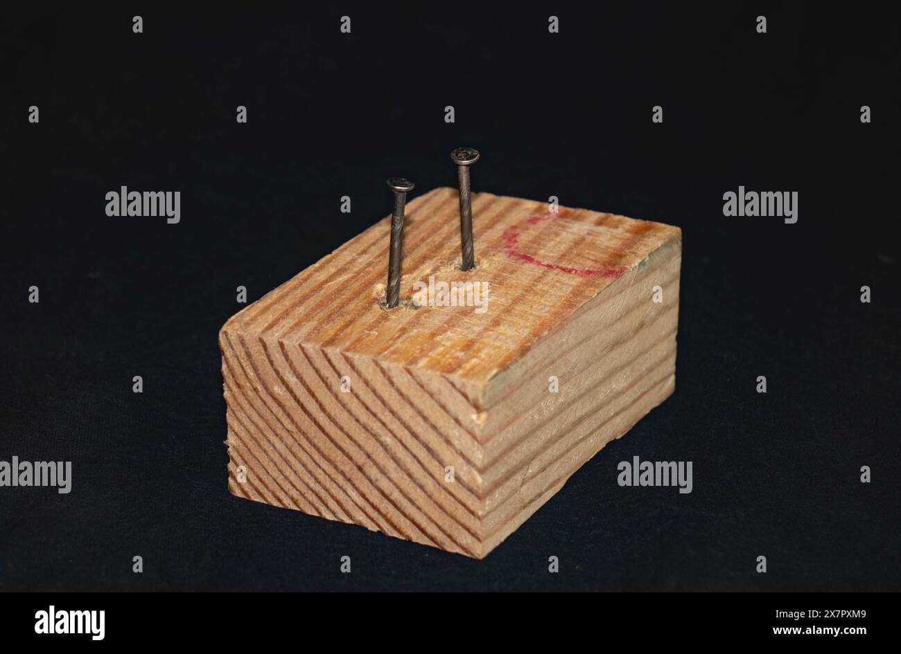a block of wood with two screw nails driven into it. Black background ...