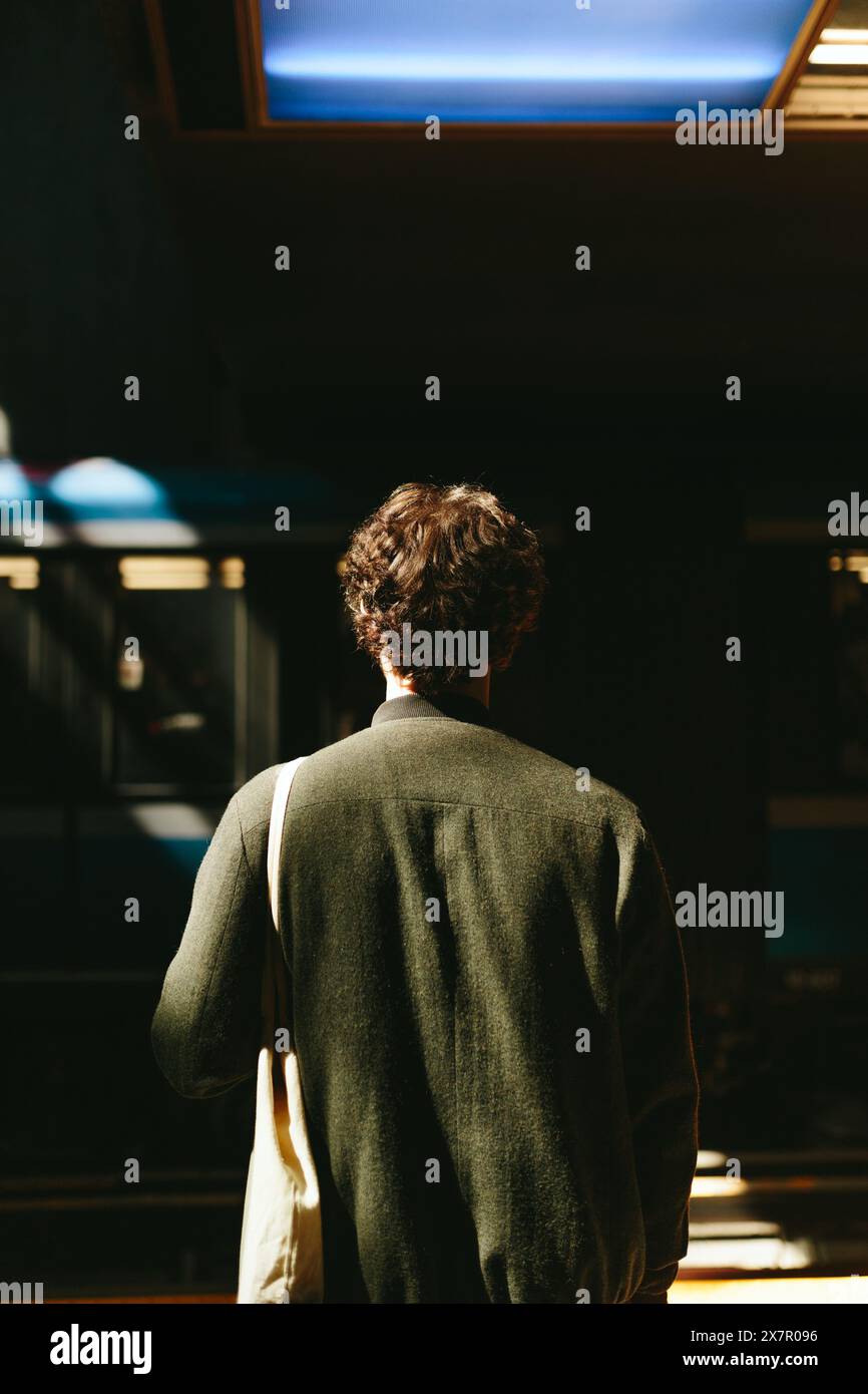 A young man stands with his back to the camera, engulfed in shadow ...