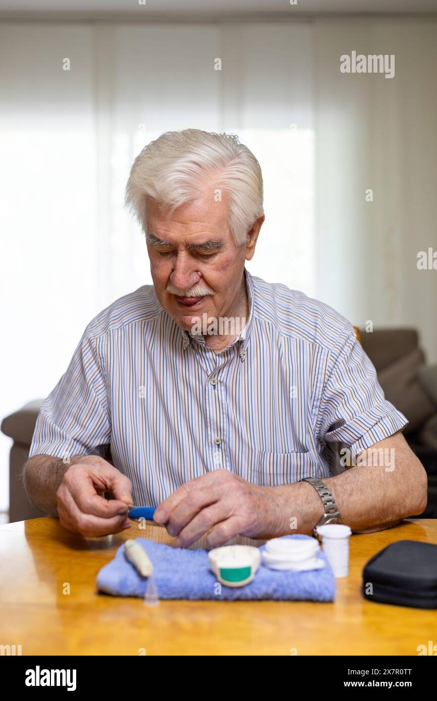 An elderly Caucasian man seated at a table, focused on monitoring his ...