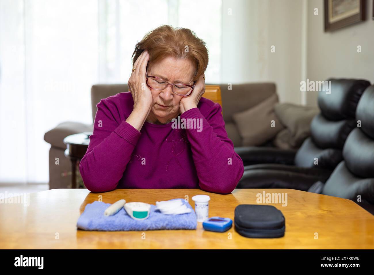 A senior woman sits at a table, appearing distressed, with her hands on ...