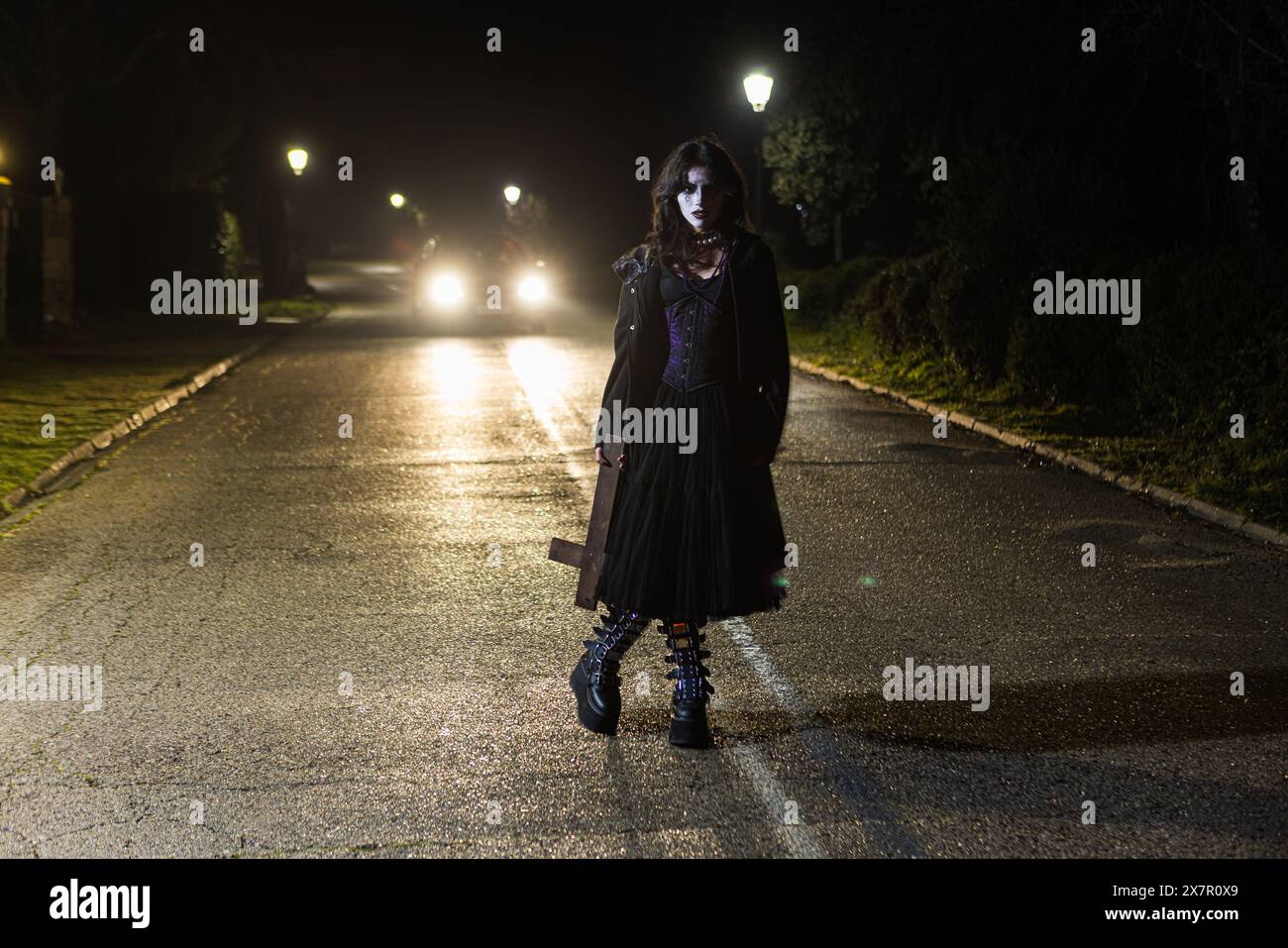 Mysterious woman dressed in a gothic style standing on a dimly lit road ...