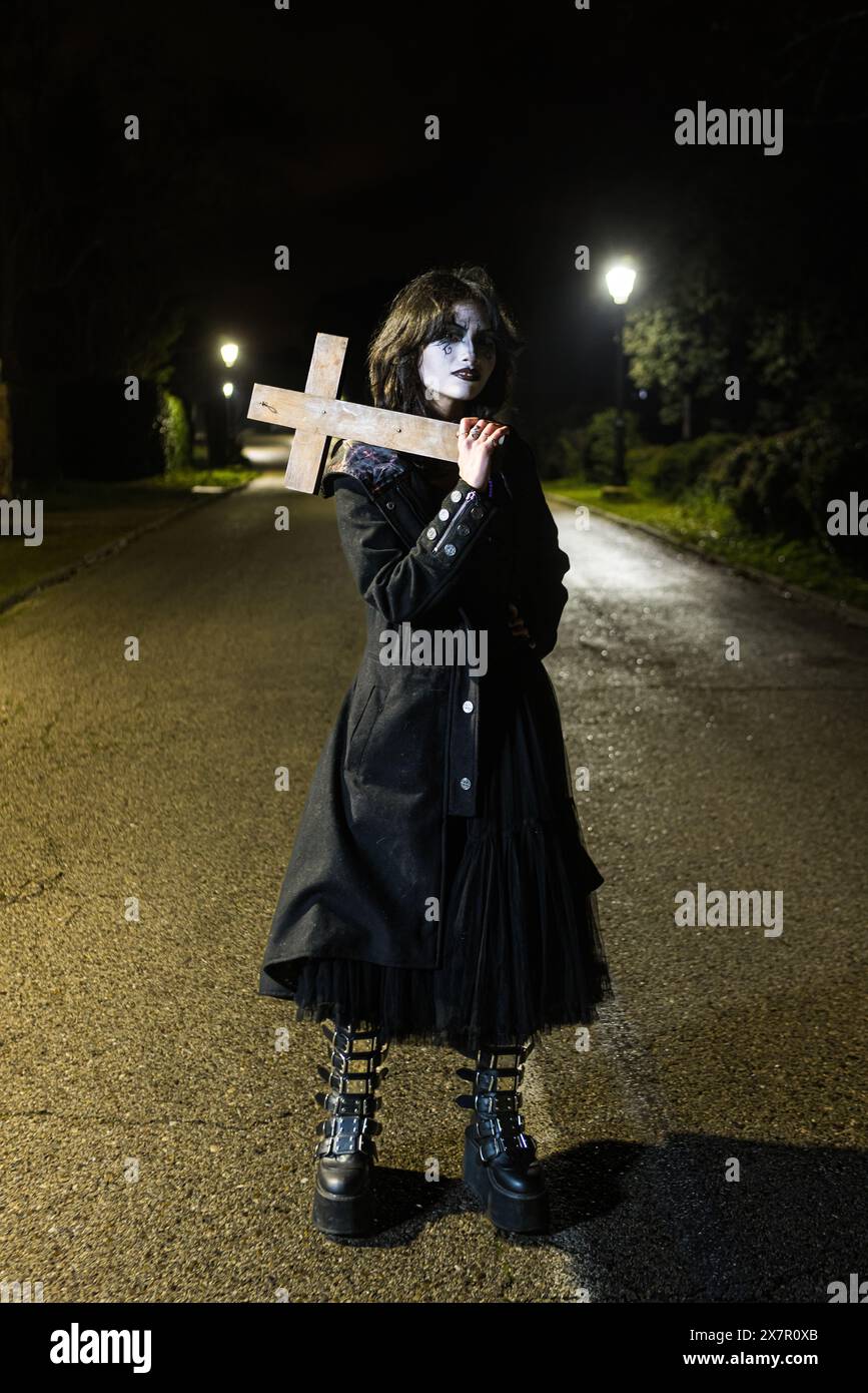 A person dressed in gothic attire with dramatic makeup holds a wooden ...