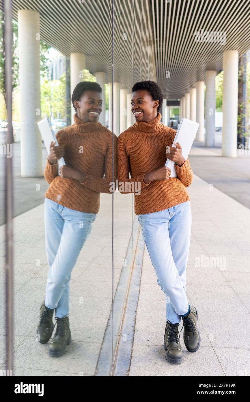 Young African female student smiles as she leans on a reflective pillar ...