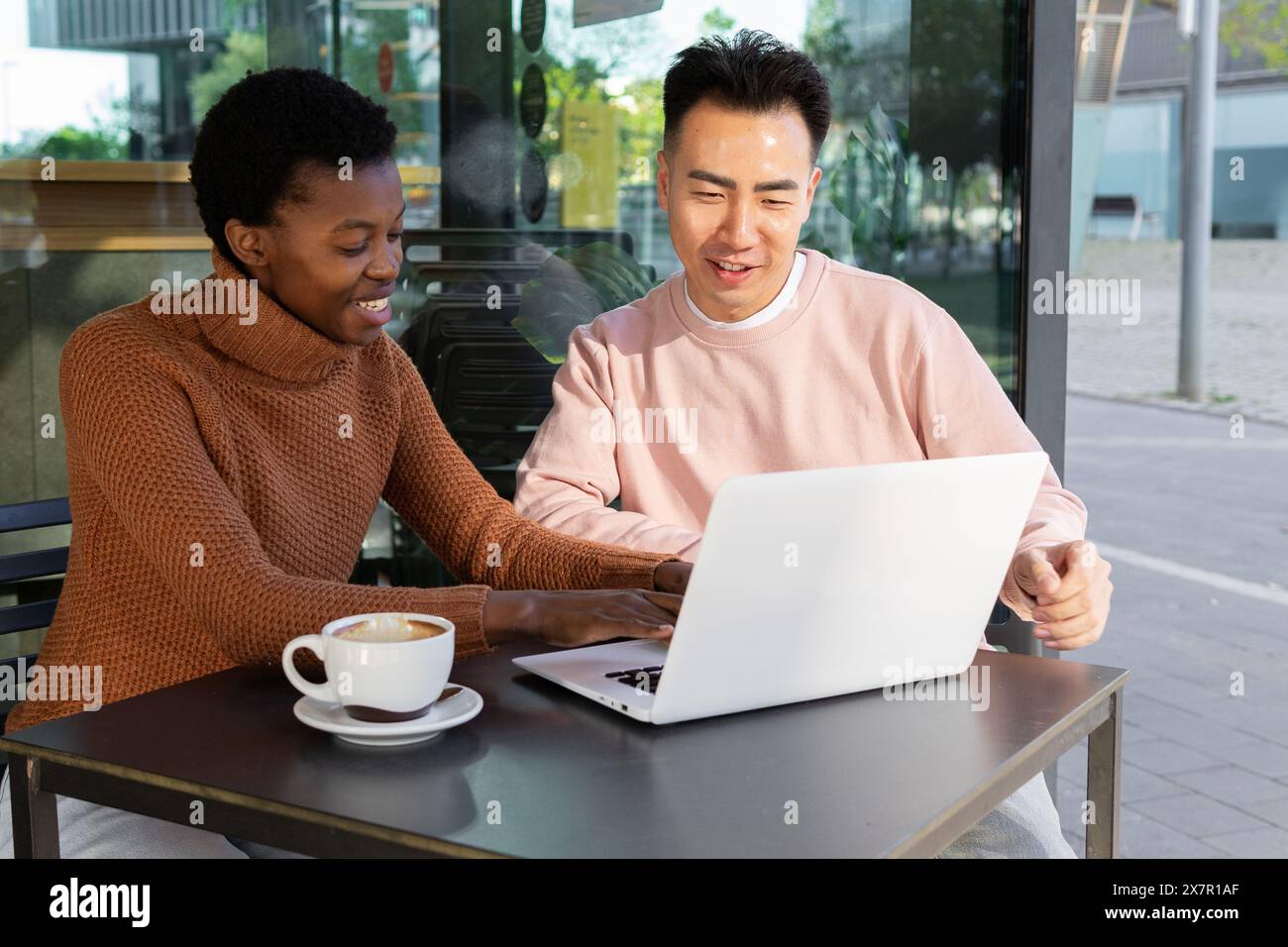 Two students, a male Asian and a female African, engaging over a laptop ...