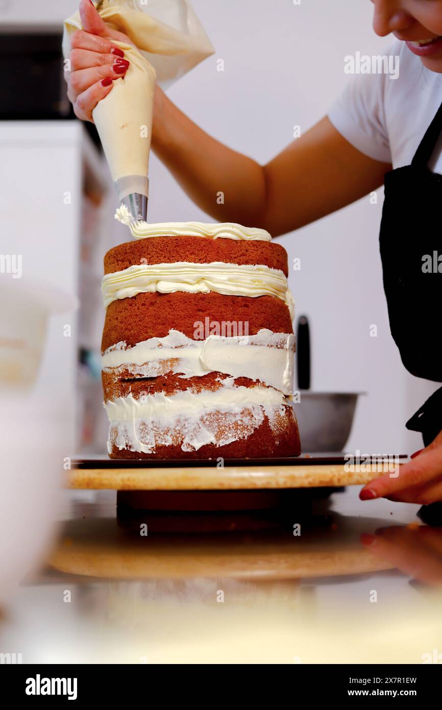Skilled baker in kitchen decorating a multi-layered sponge cake with ...