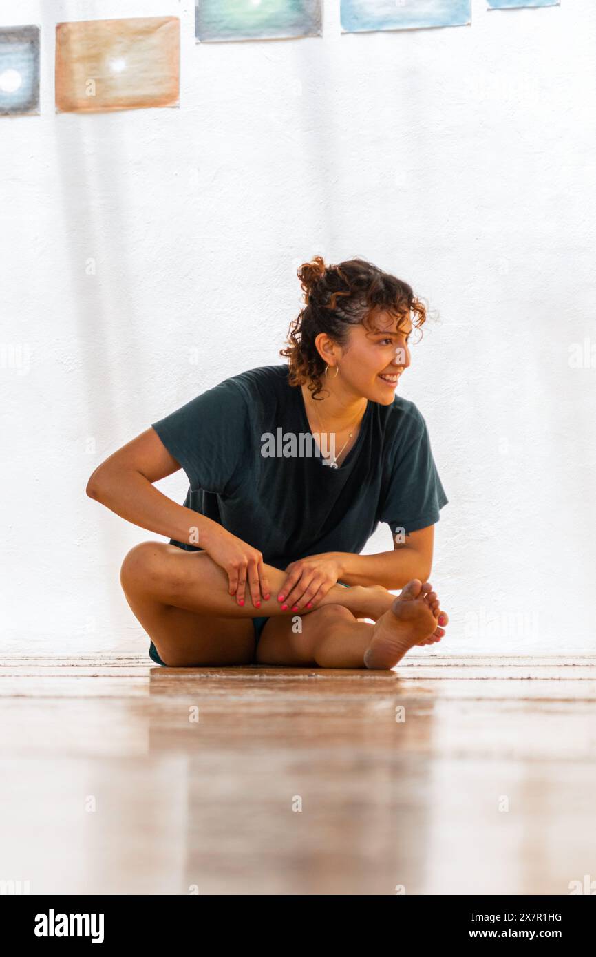 A woman with a joyful expression sits on a wooden floor, stretching in ...