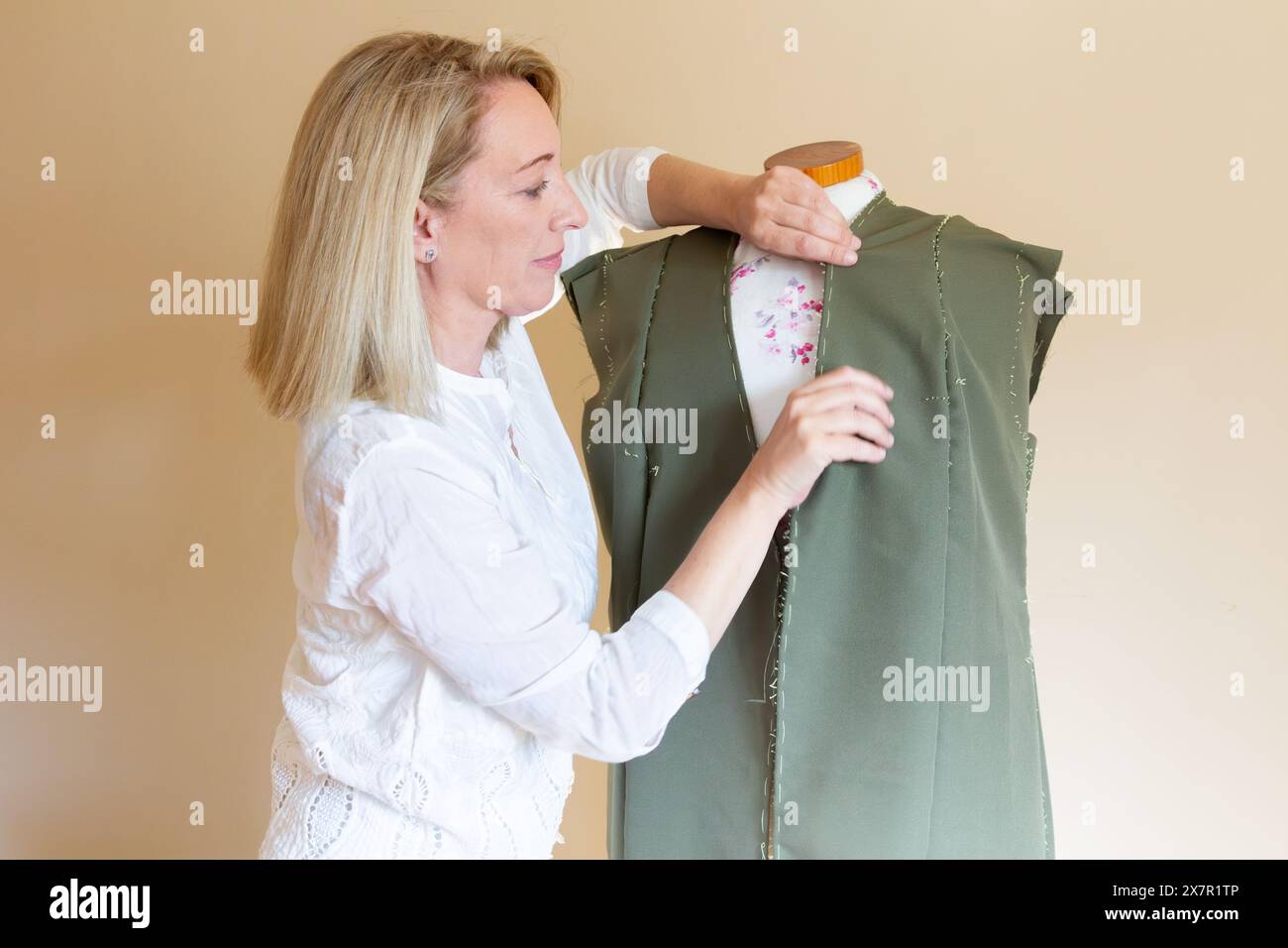 A female tailor attentively adjusts a green garment on a dress form ...