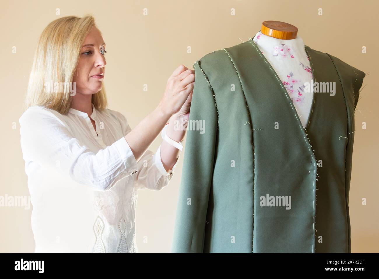 Female tailor in white blouse meticulously adjusting a green jacket on ...