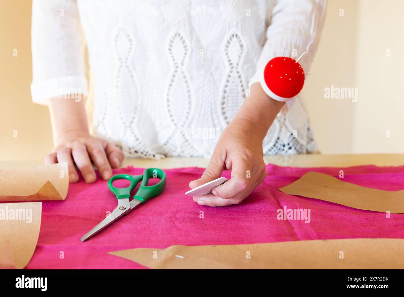 Close up of a tailor's hands tracing a paper pattern onto vibrant pink ...
