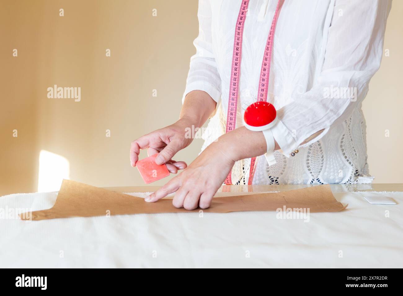 A tailor with a measuring tape around her neck is marking a pattern on ...