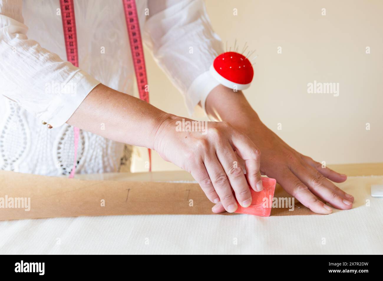 A tailor with a measuring tape around her neck is marking a pattern on ...