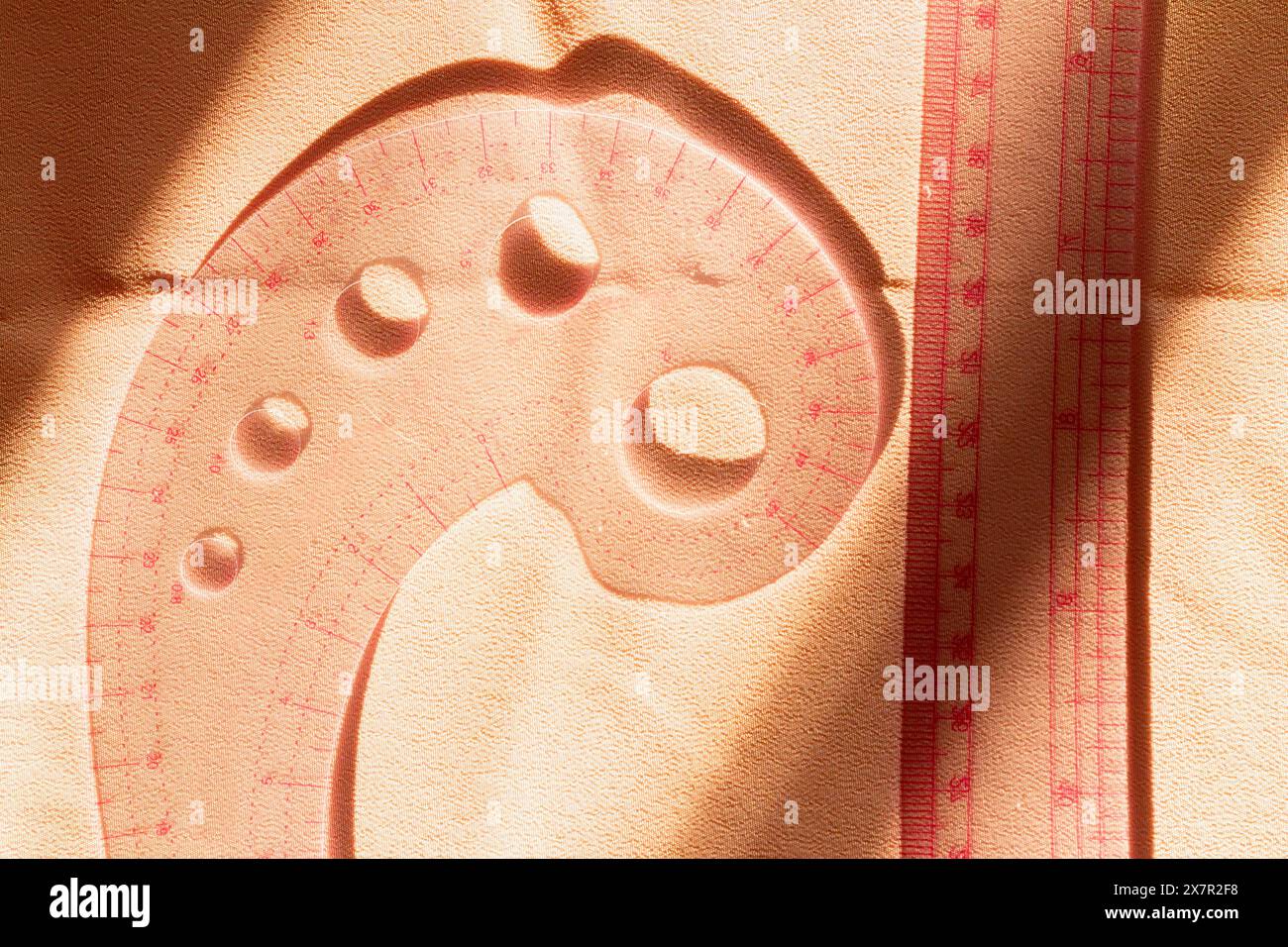 Sunlight casts shadows of a French curve and ruler on a textured fabric ...
