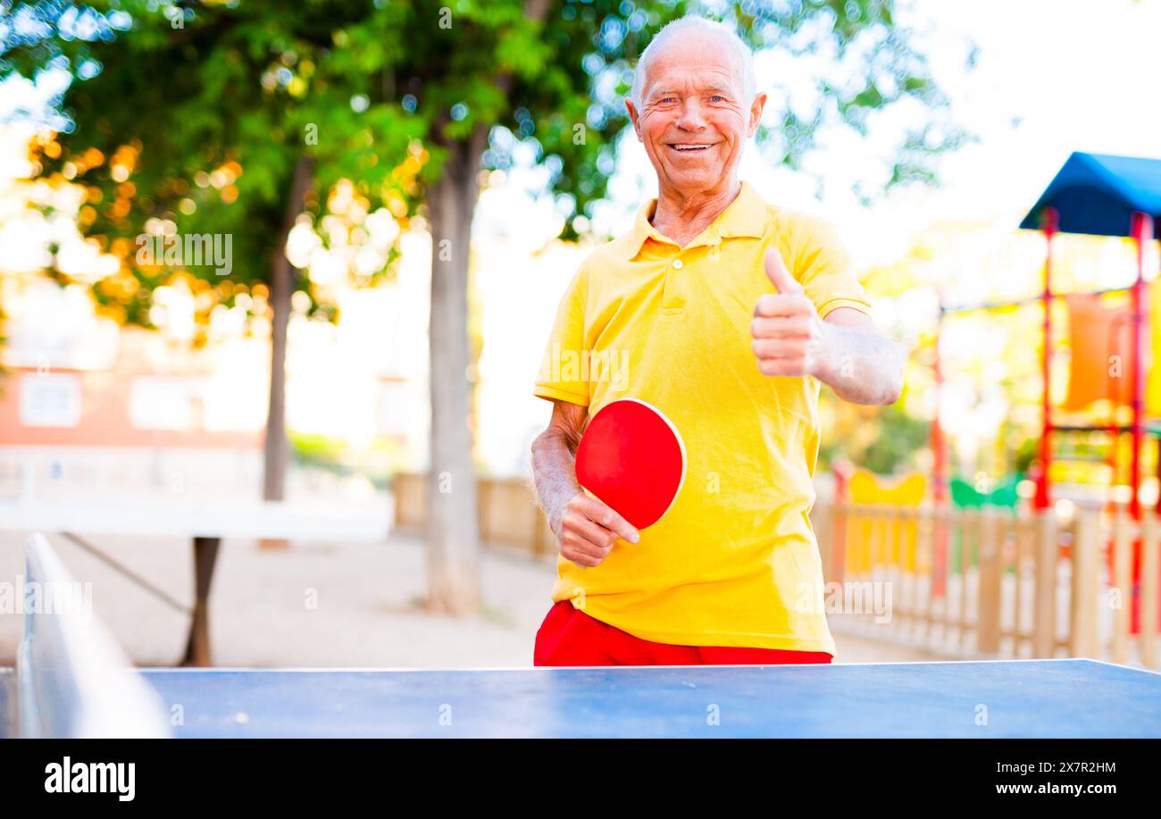Portrait of elderly man with rackets for table tennis showing thumb up ...