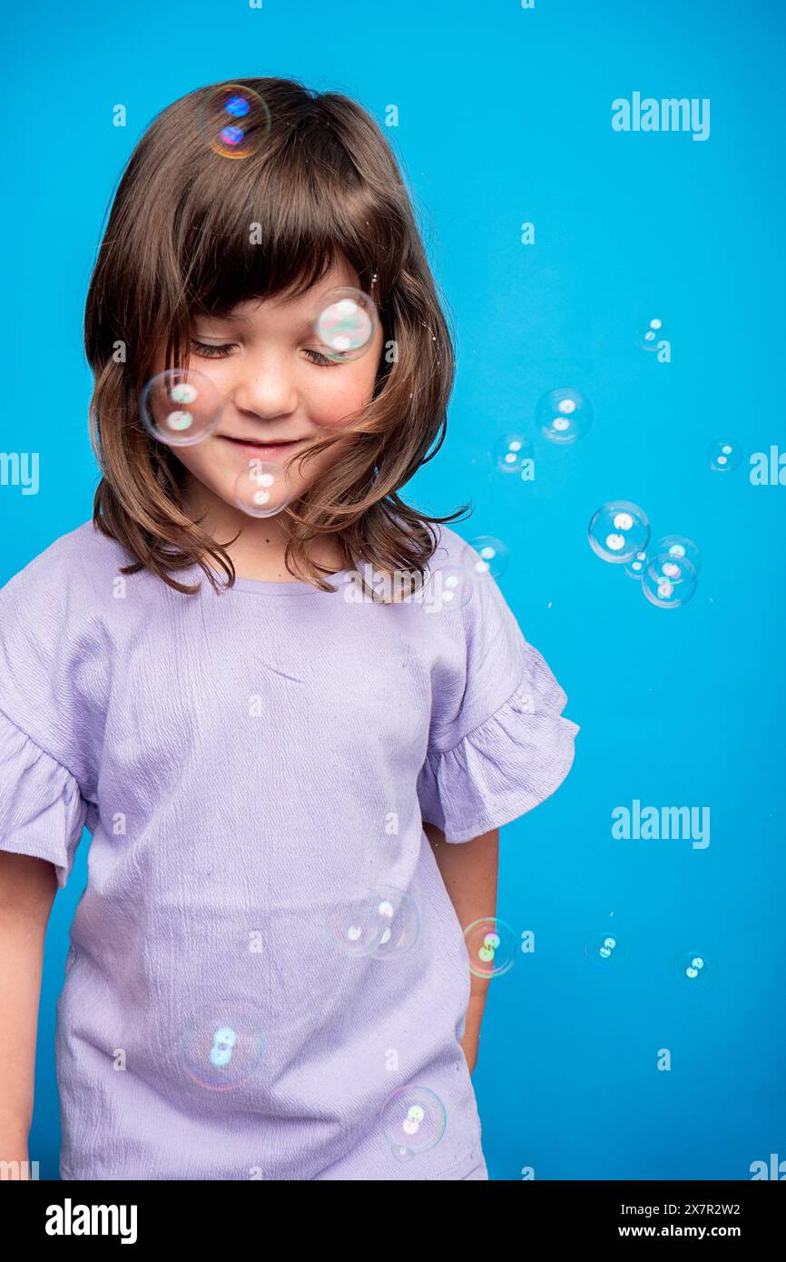 A cheerful young girl looking down with a subtle smile as soap bubbles ...