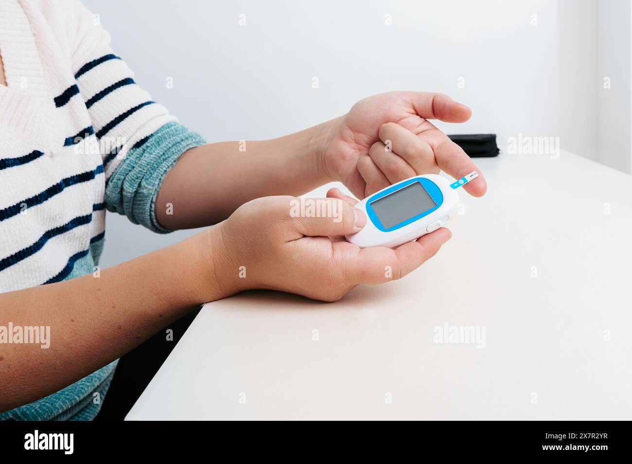 A close-up of hands using a digital glucometer to check blood sugar ...