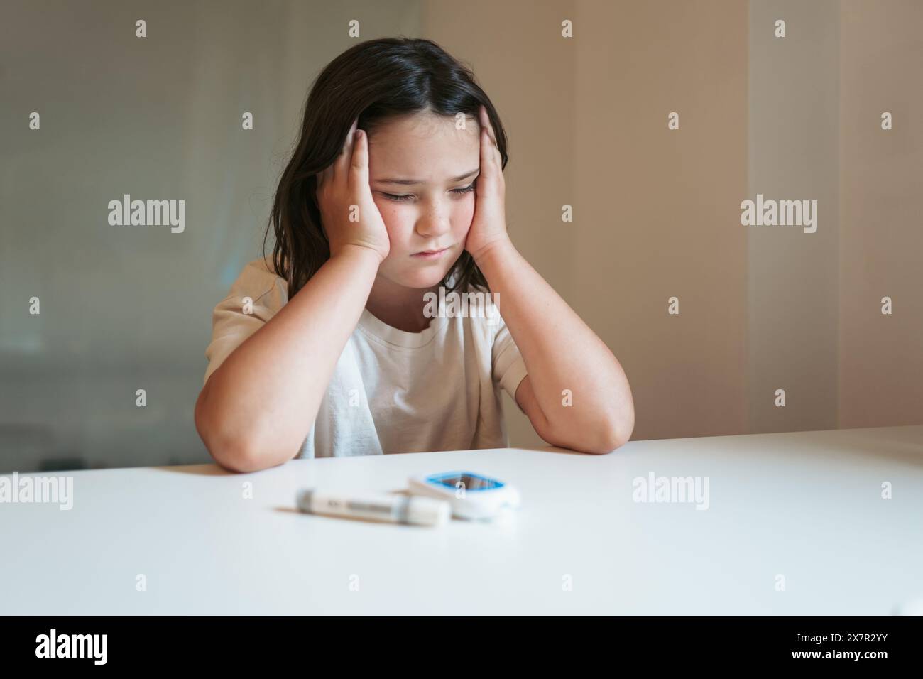 A young girl sits at a table, appearing distressed with her hands on ...