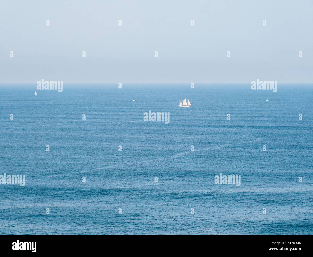 Calm blue sea under a hazy sky, dotted with small sailboats on the ...