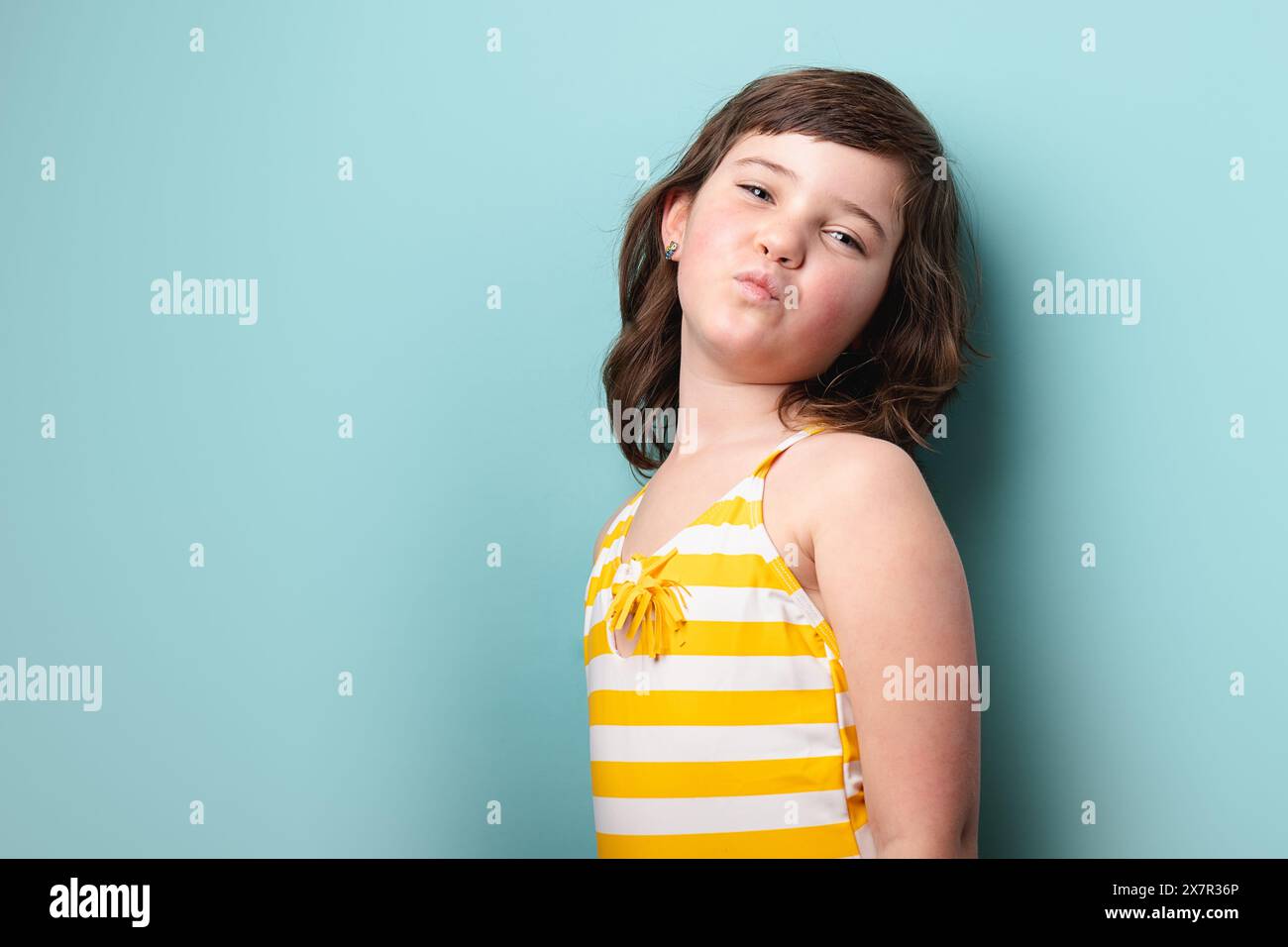 A young girl in a yellow and white striped swimsuit stands against a ...